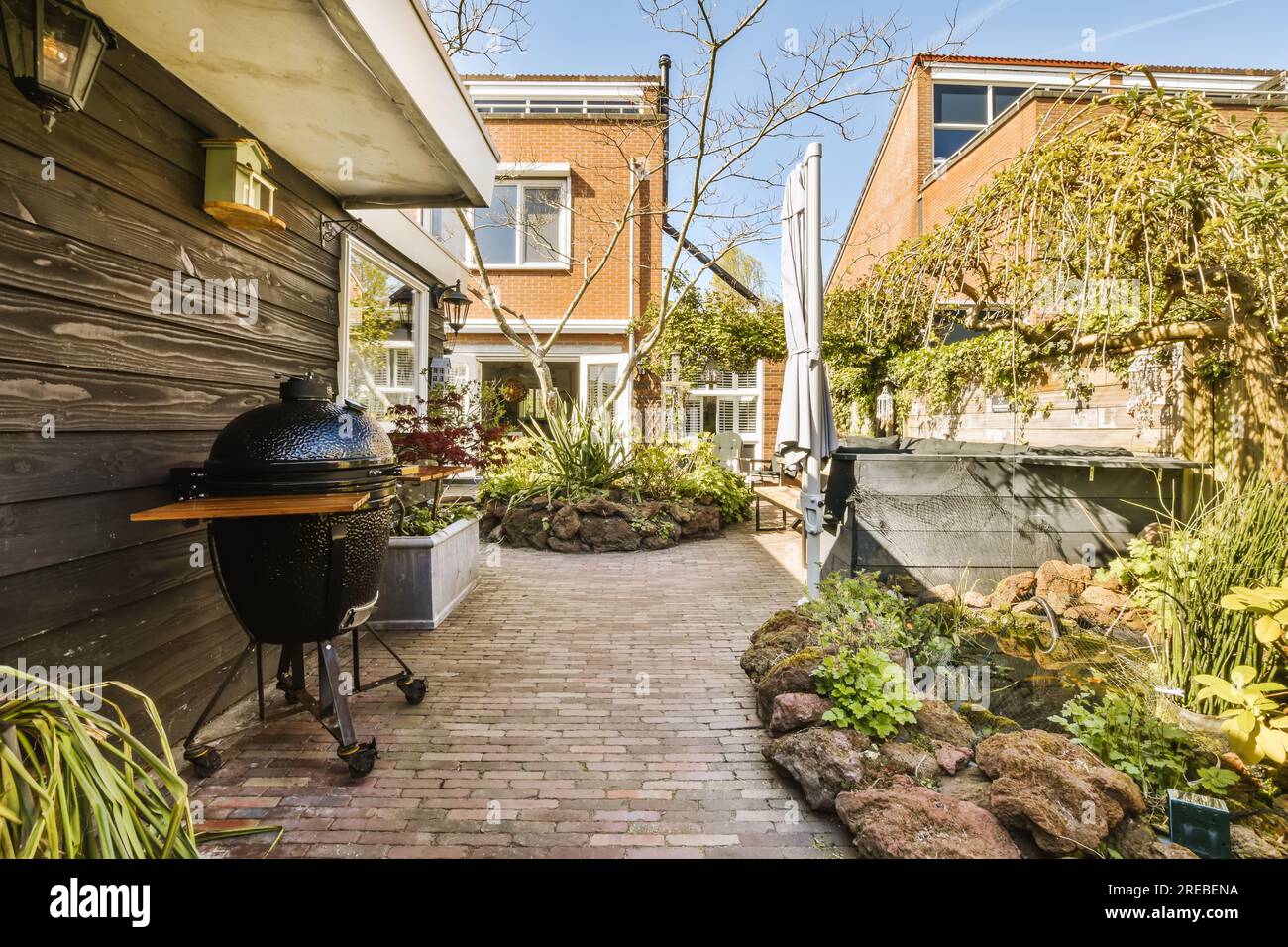 a back yard with some plants on the left side and a grill in the middle ...