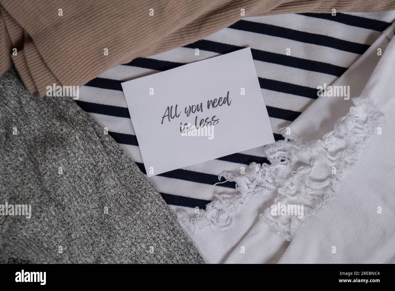 ALL YOU NEED IS LESS text on paper note on clothes assortment Second ...