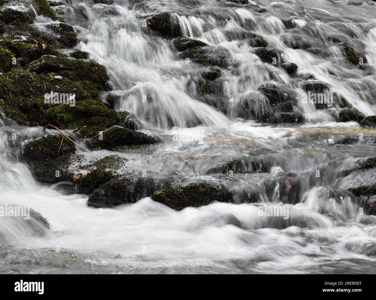Water flowing over moss covered rocks forming a shallow waterfall Stock ...