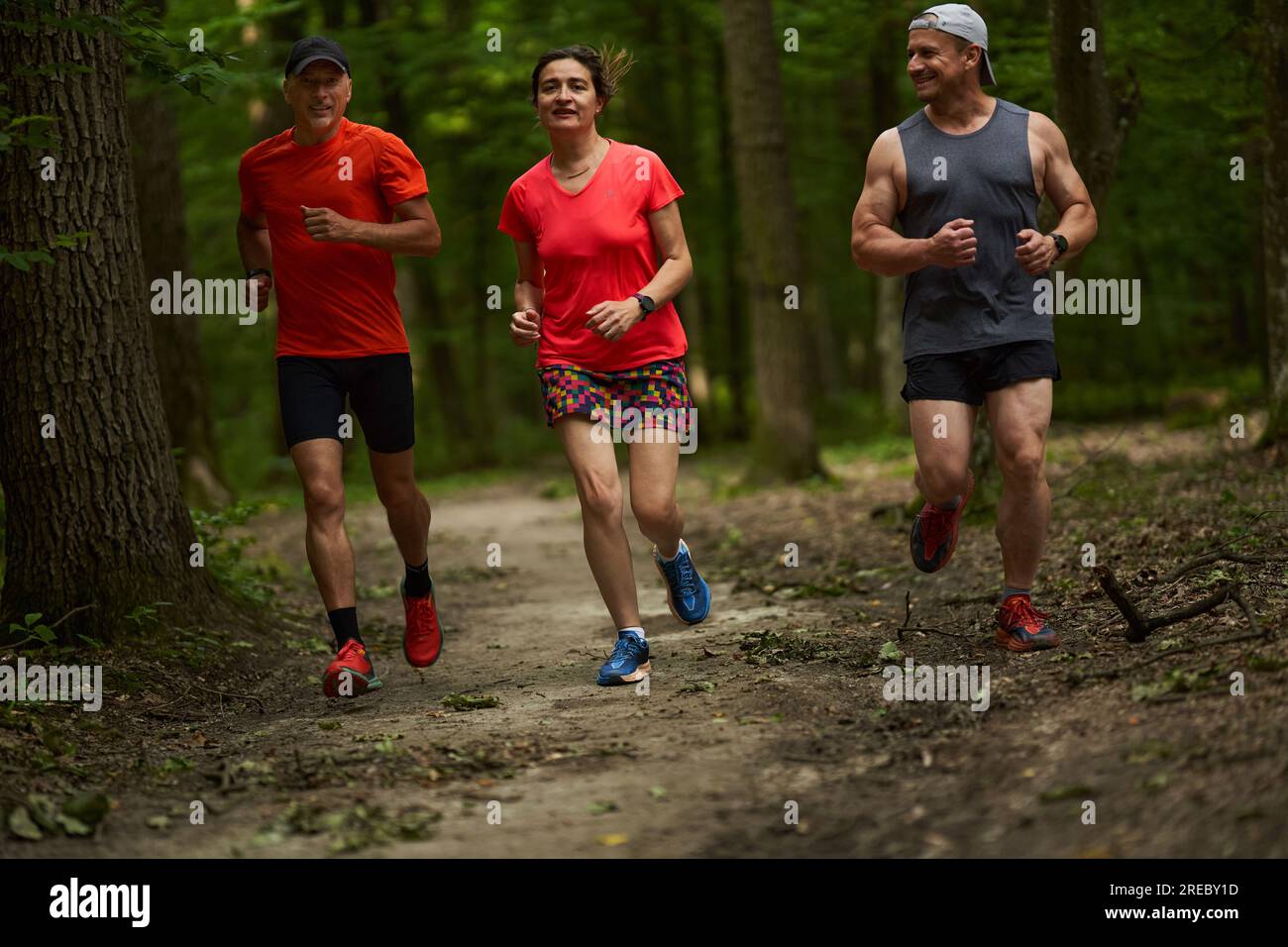 A group of three runners, jogging on a running trail through the forest ...