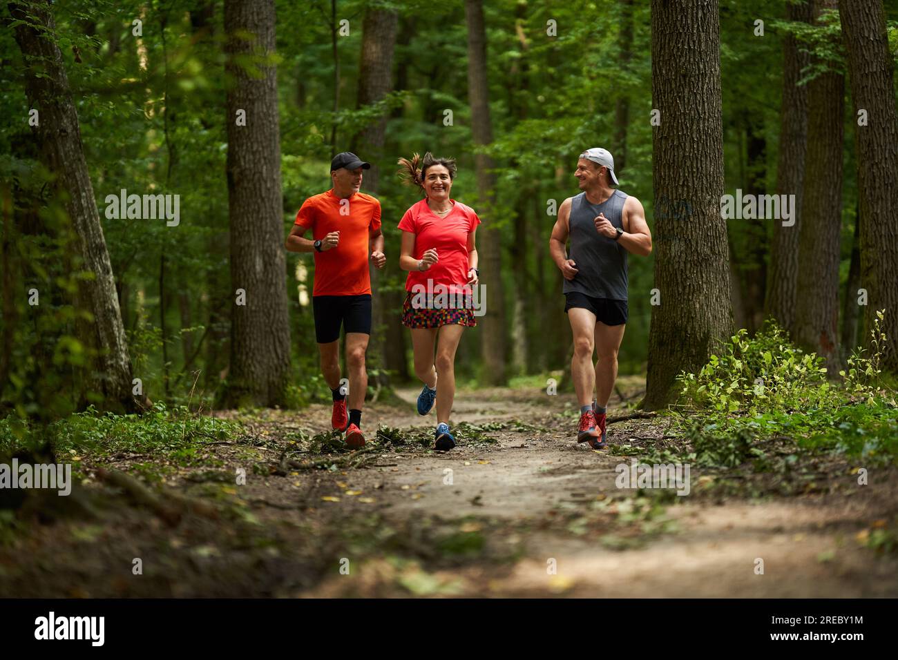 A group of three runners, jogging on a running trail through the forest ...