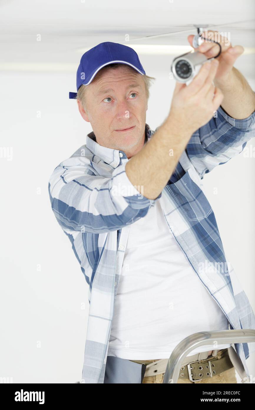 mature handyman on stepladder fitting cctv camera to ceiling Stock ...