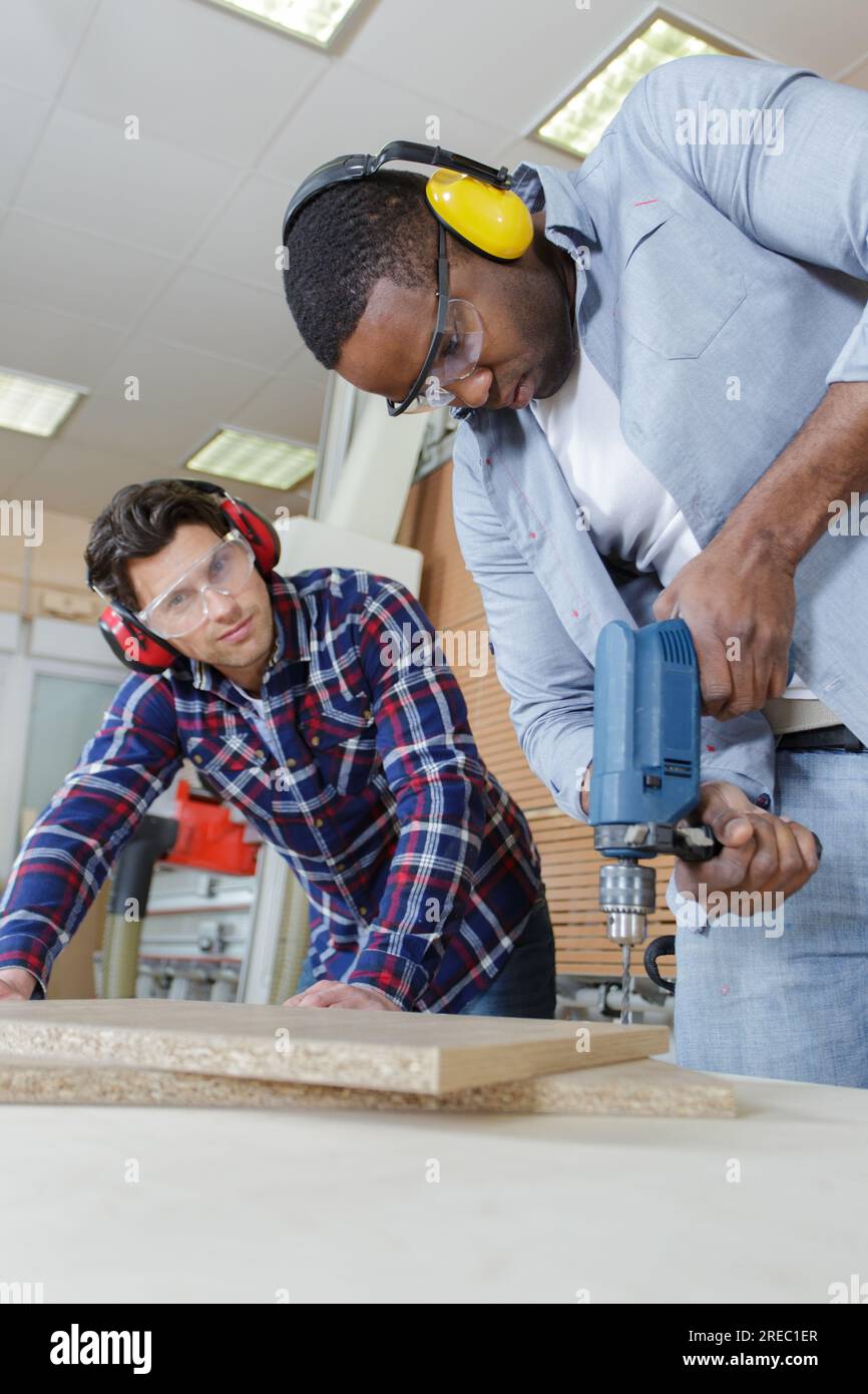 engineer training male apprentice using a drill press Stock Photo - Alamy