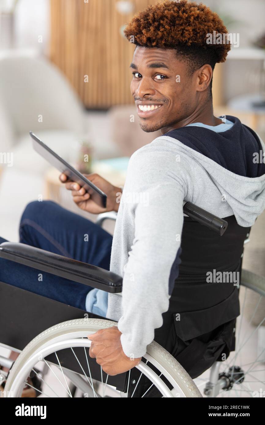 Disabled Man In Wheelchair Holds Tablet And Smiles At Camera Stock