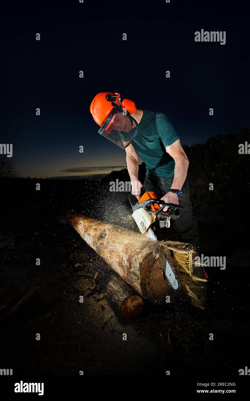 A Man cutting a tree trunk in half lengthways with a chainsaw under a ...