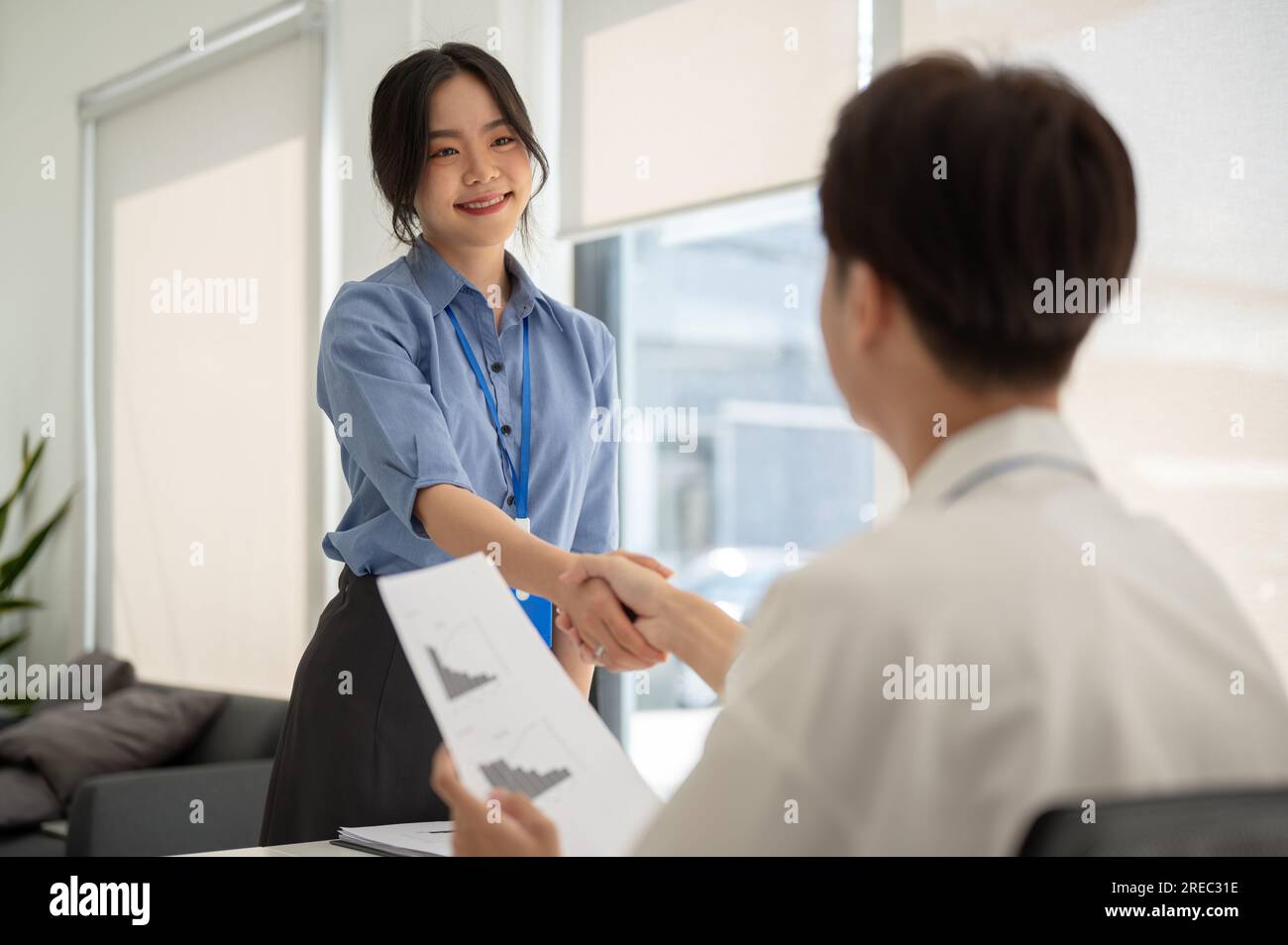 An attractive and happy Asian businesswoman shakes hands with a male ...