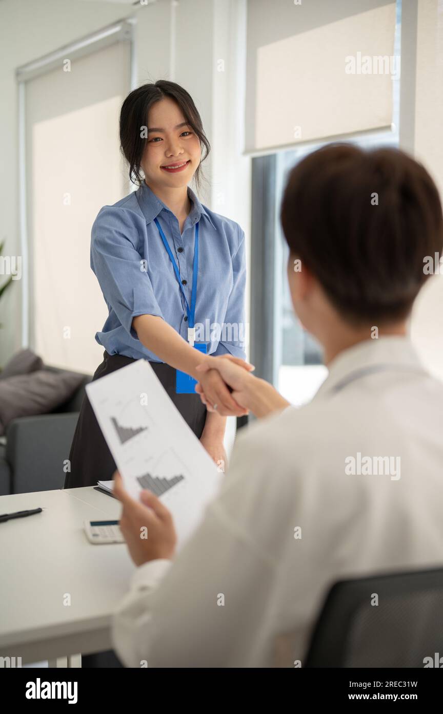 A portrait of a beautiful Asian businesswoman shakes hands with a male ...