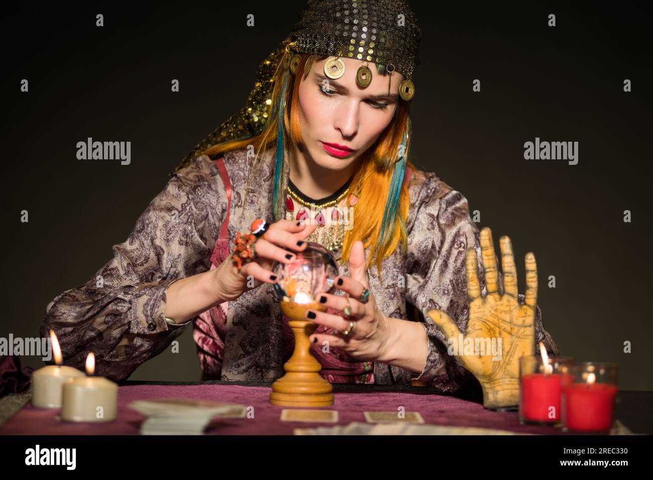 Concentrated young female fortune teller with long ginger hair in dress ...