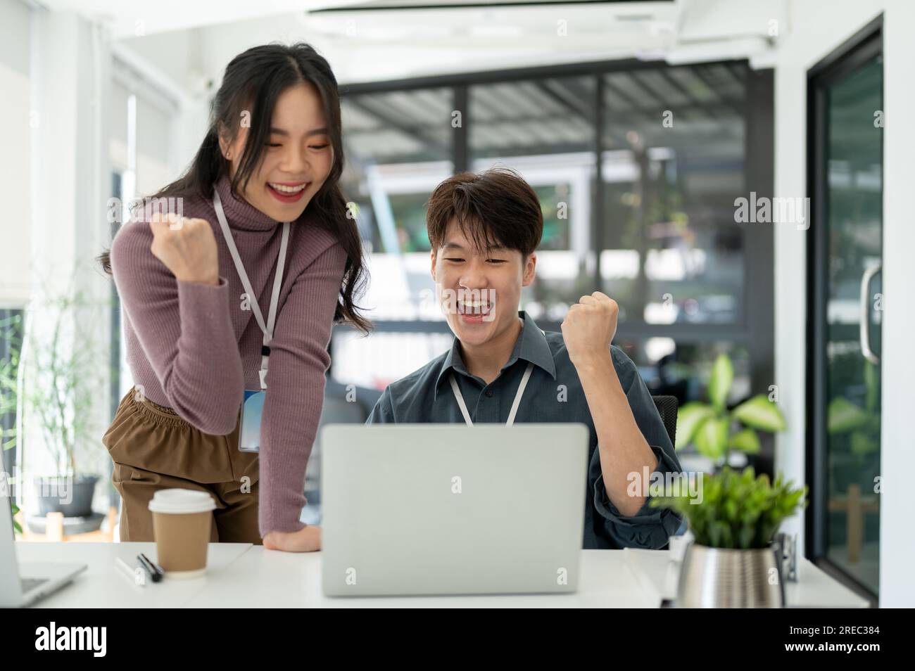 Two cheerful and happy young Asian office employees are looking at a ...