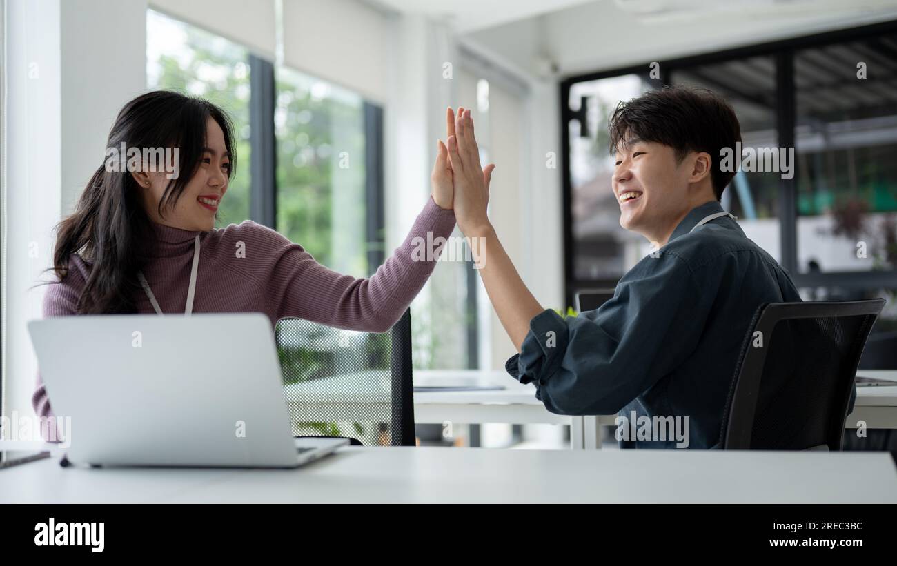 Two cheerful and happy young Asian workers give high fives to each ...