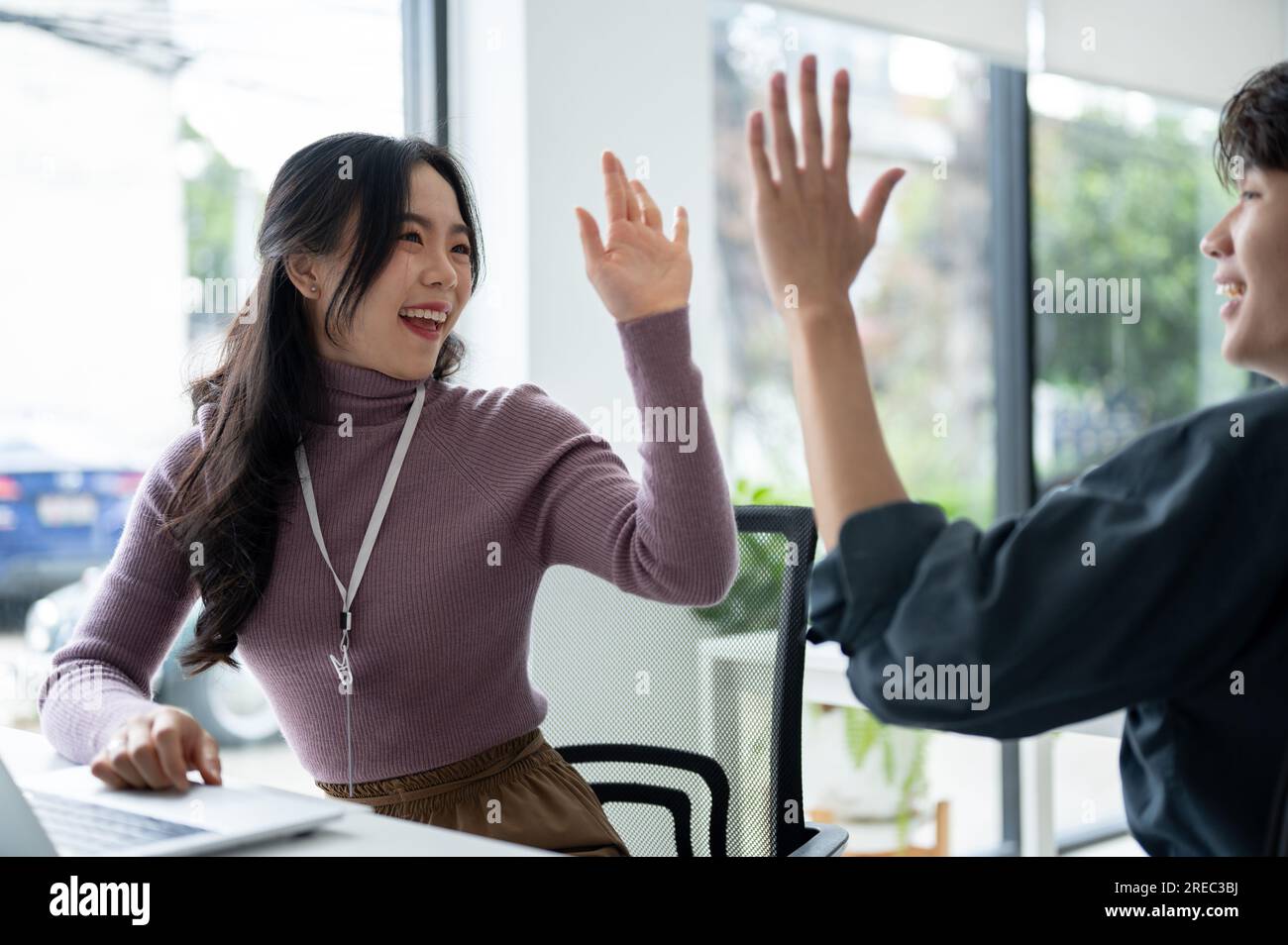 A cheerful and beautiful young Asian female worker gives high fives to ...