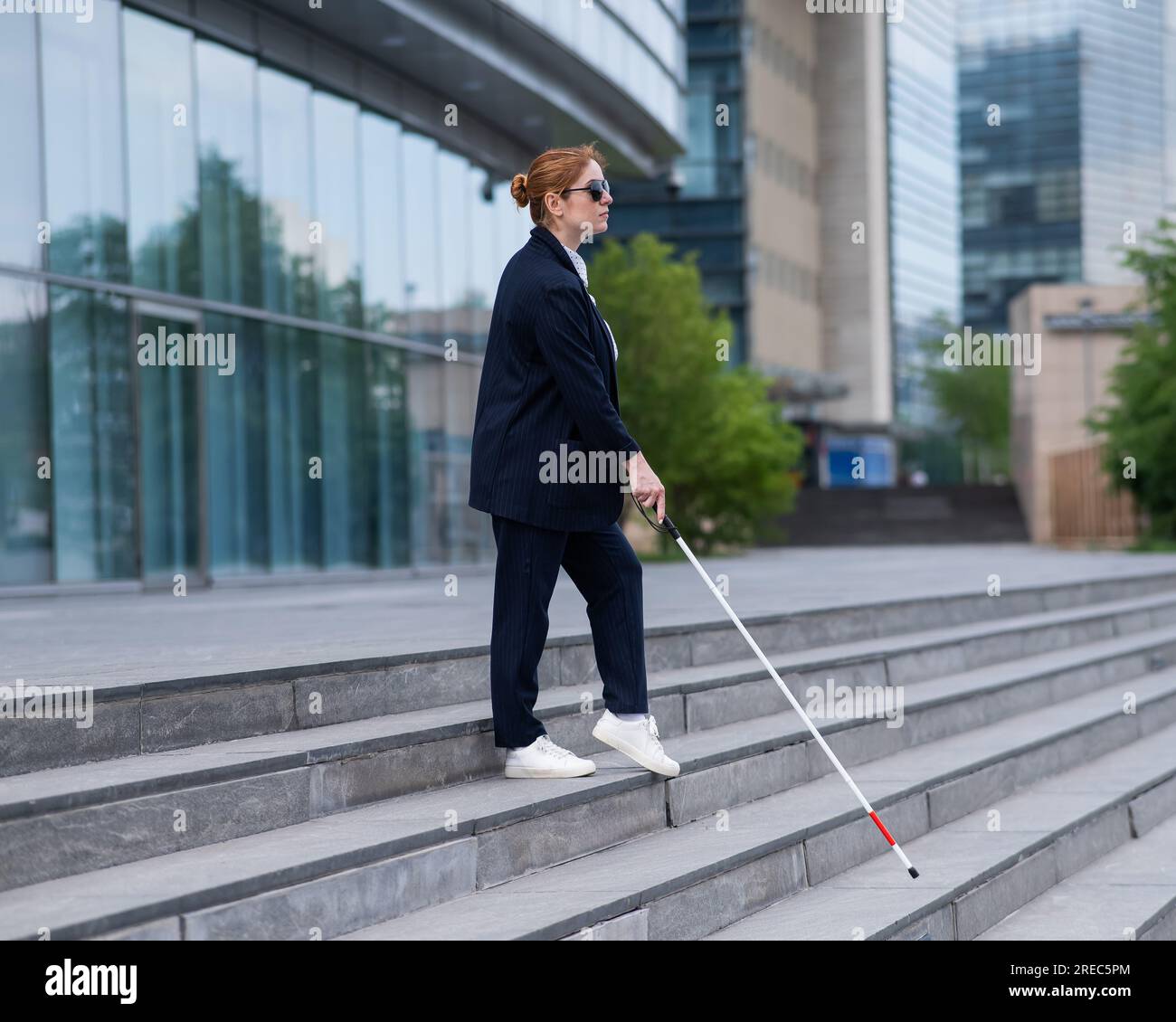 Blind business woman descending stairs with a tactile cane from a ...
