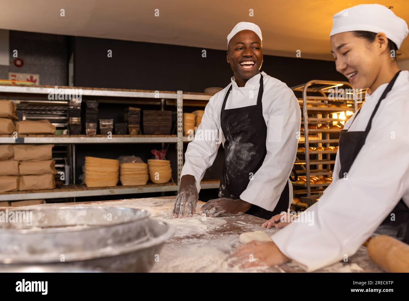 Happy diverse bakers wearing aprons in bakery kitchen and preparing ...