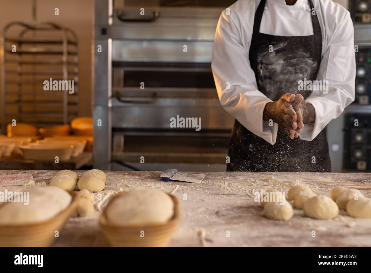 African american male baker in bakery kitchen clapping hands with flour ...