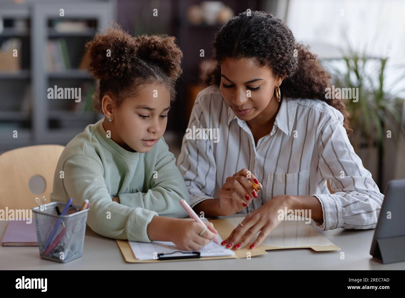 Portrait of cute black girl doing homework with mother or tutor helping ...