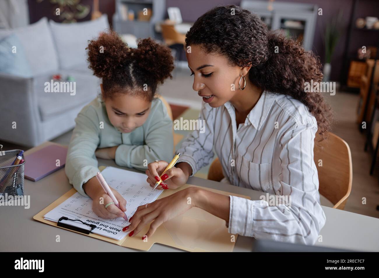 Portrait of black young woman explaining math to little girl in home ...