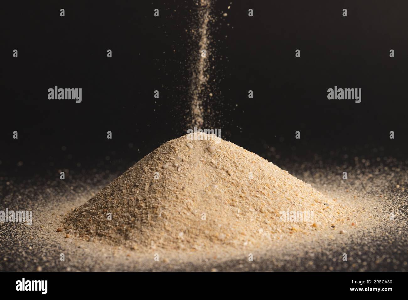 Close up of sand pouring into heap and copy space on black background ...