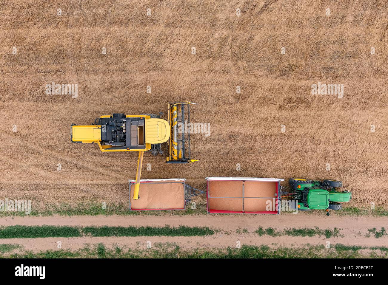 Tractor with trailer working in tandem alongside a working combine ...