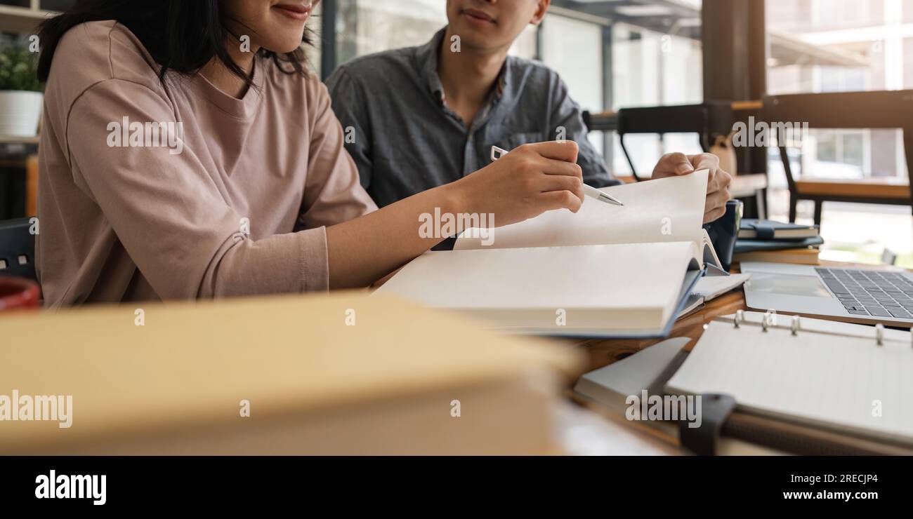Two asian male and female students college sitting at desk in library ...