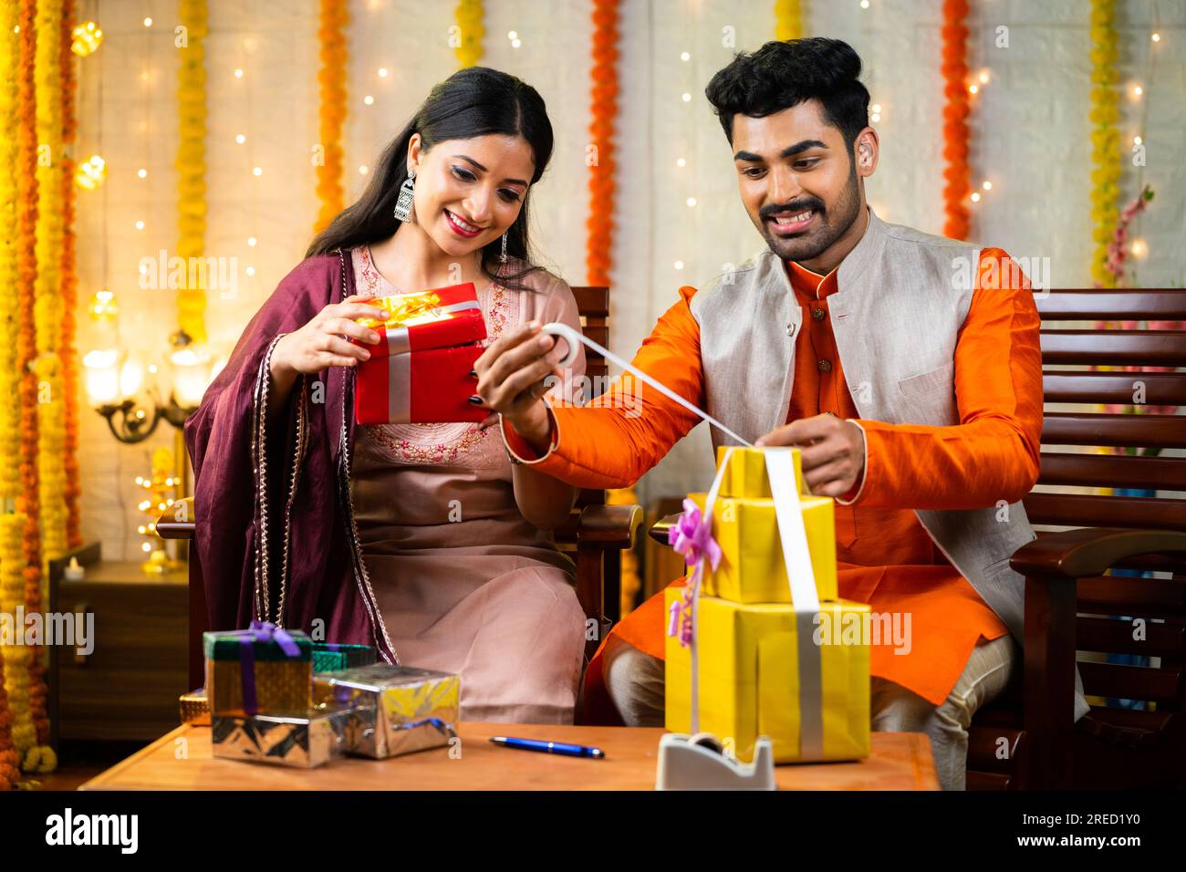Happy young indian couple packing gift boxes for festival celebration at home - concept of ...
