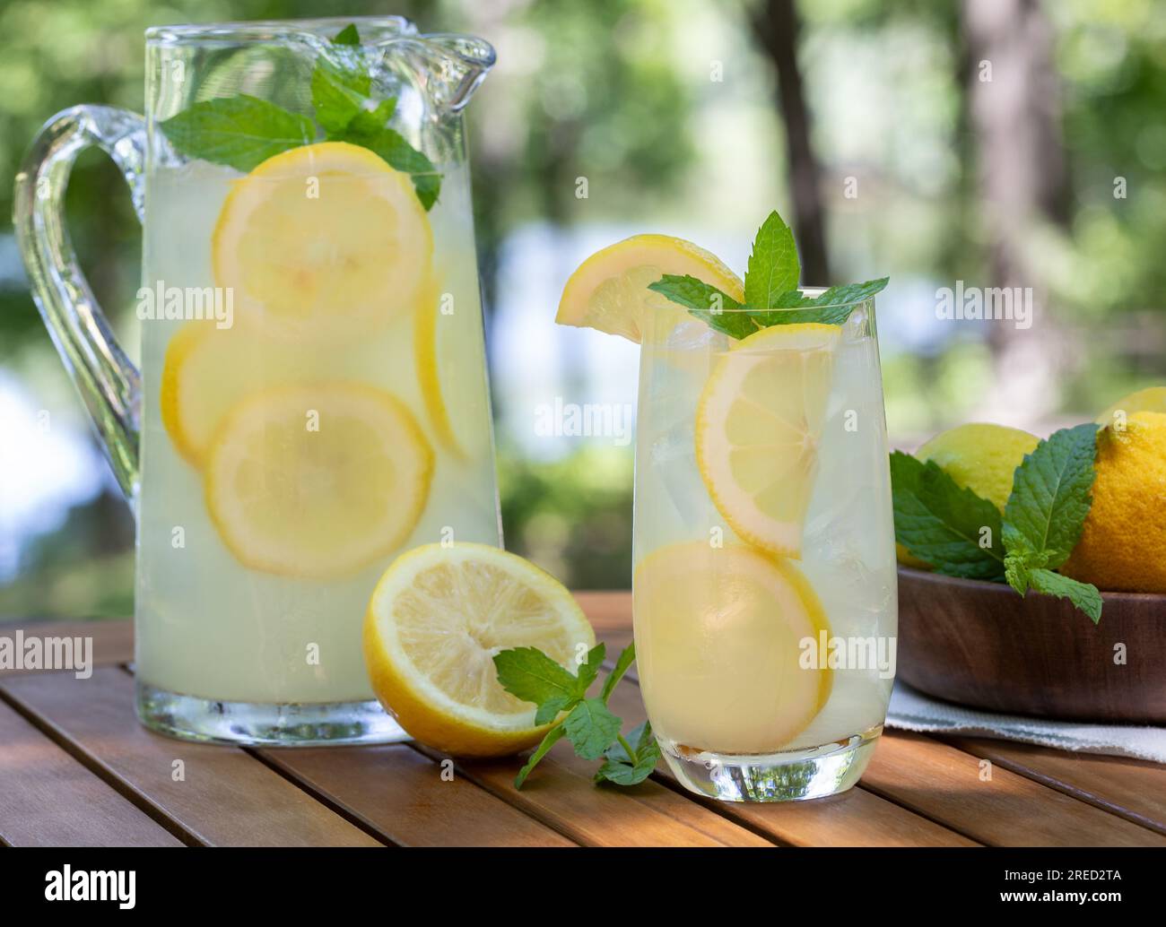 Lemonade in glass and pitcher with mint and sliced lemons outdoors on ...