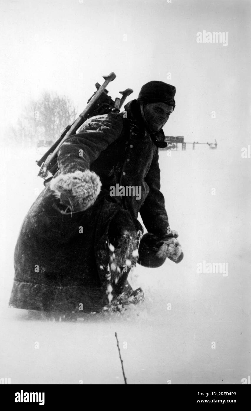 German soldier trudges forward with his load, a machine gun mount ...