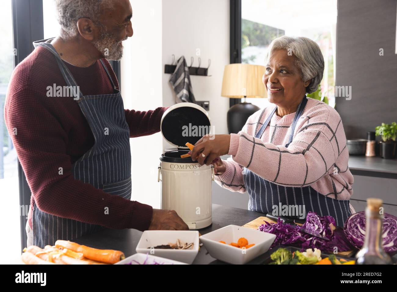 Senior biracial couple wearing aprons composting food waste in kitchen ...