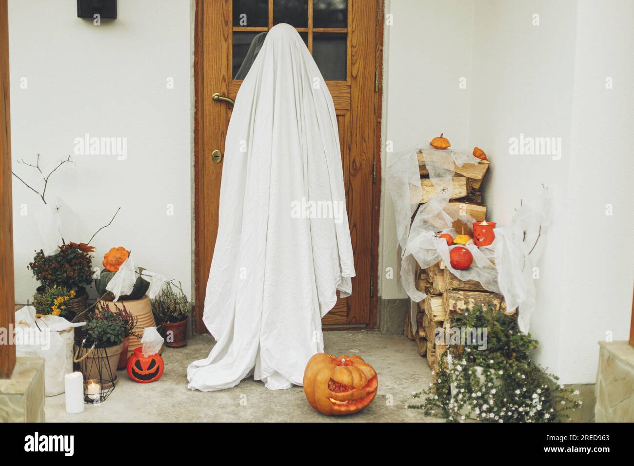 Trick or treat! Spooky ghost standing at front of house with Jack o ...