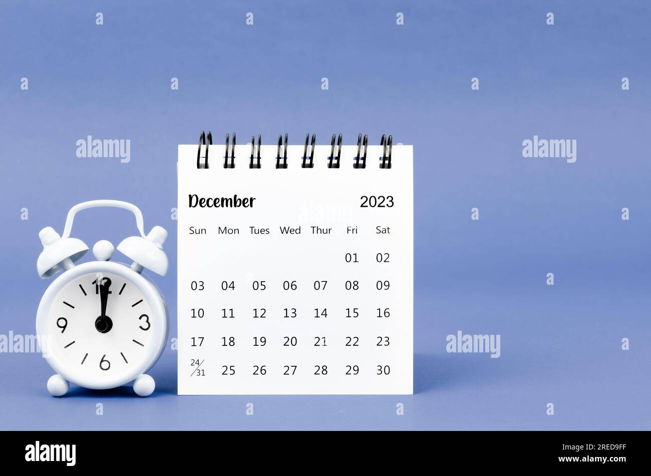 December 2023 desk calendar and alarm clock on blue color background ...
