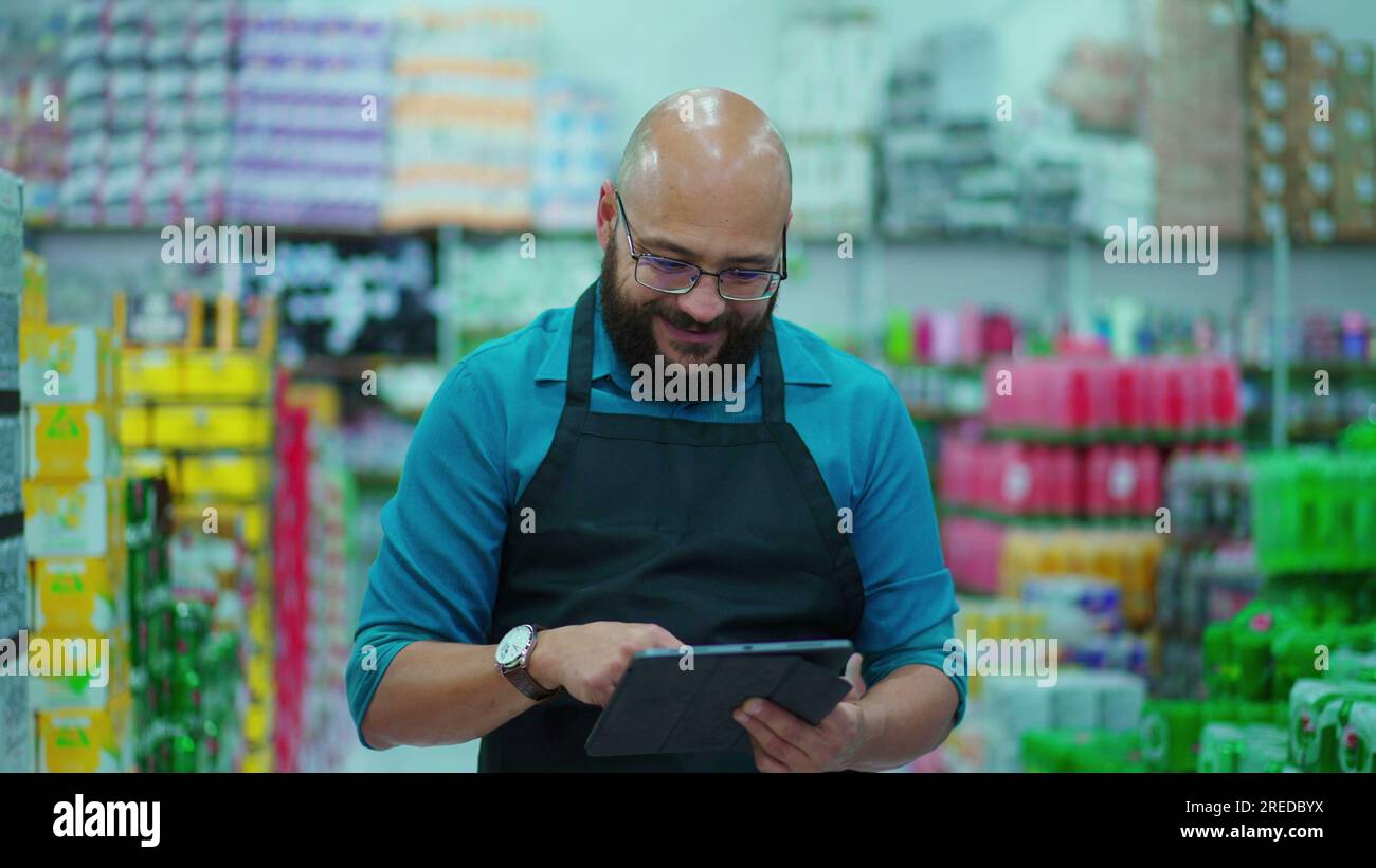 Happy employee of supermarket walking in grocery store aisle holding ...