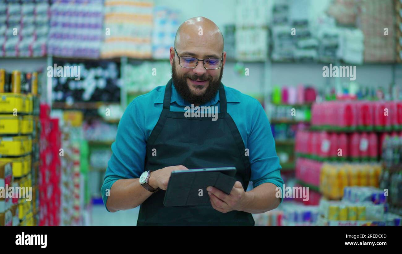Happy employee of supermarket walking in grocery store aisle holding ...