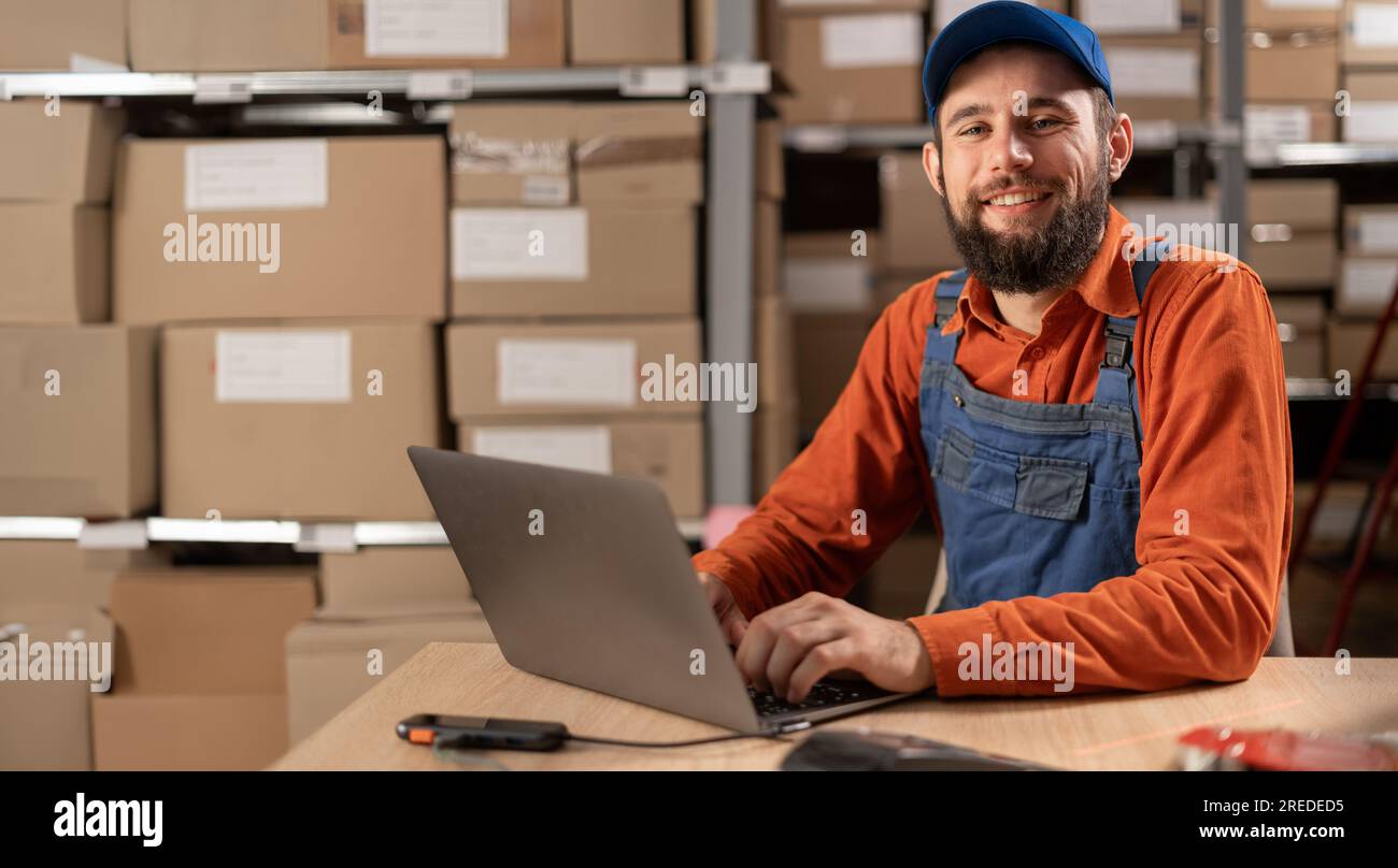 Portrait of a happy young male worker working on laptop in warehouse ...