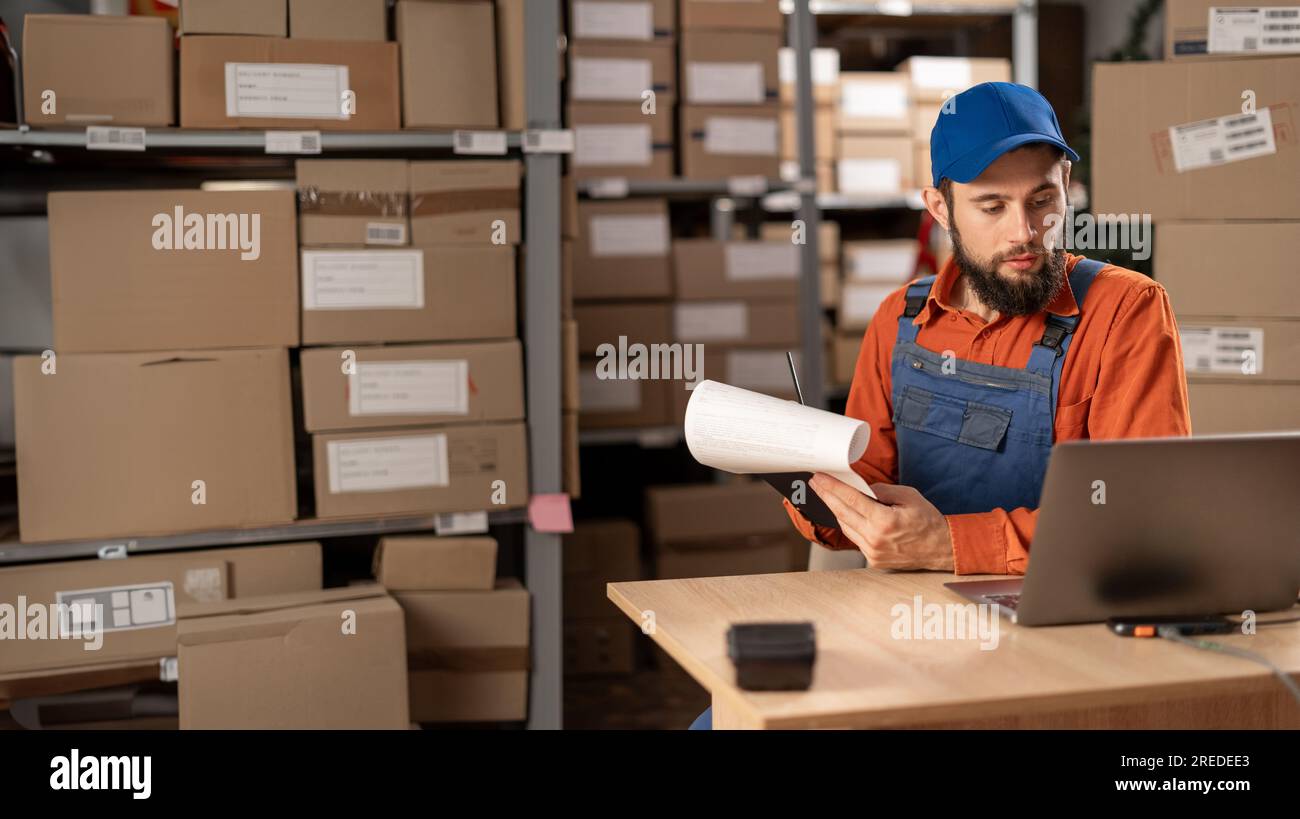 Warehouse manager using laptop and clipboard working with check list of ...