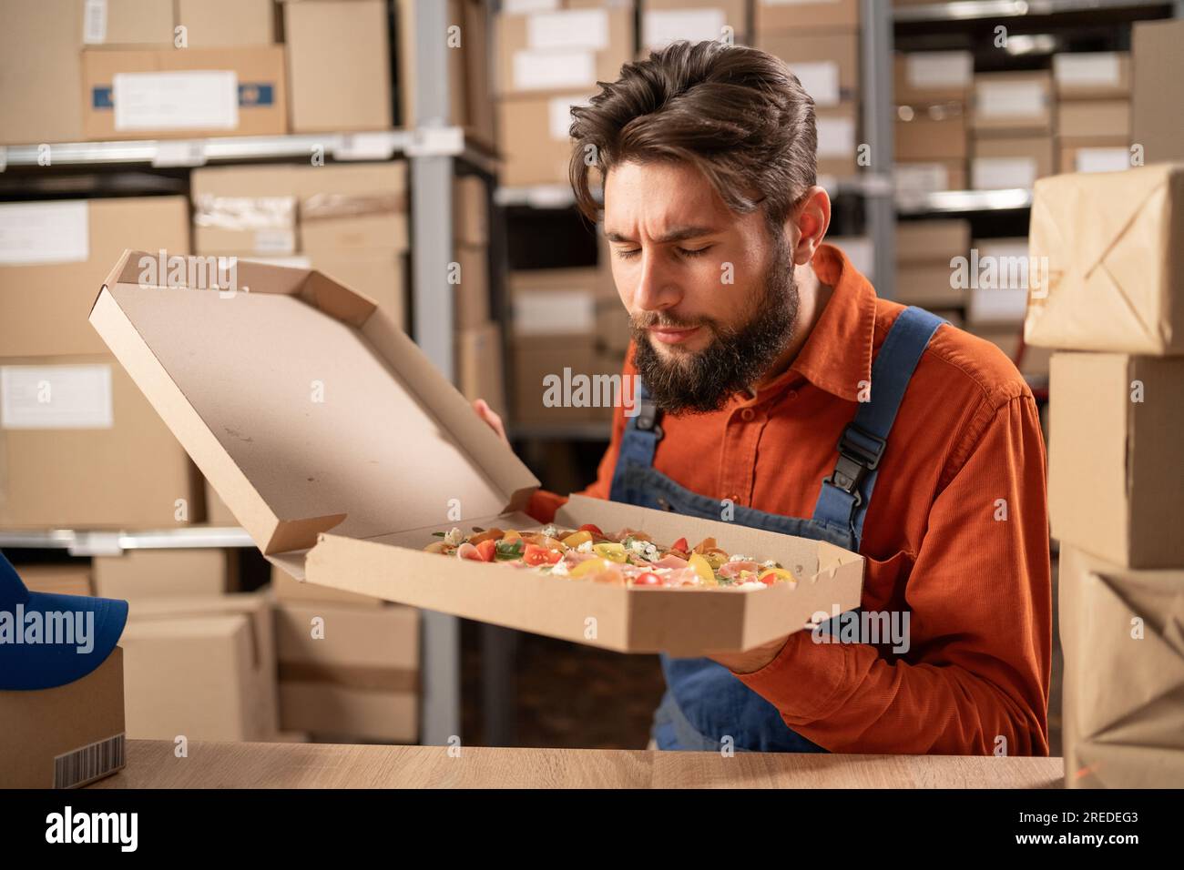 Male staff smiling while holding delicious pizza in warehouse. Lunch in ...