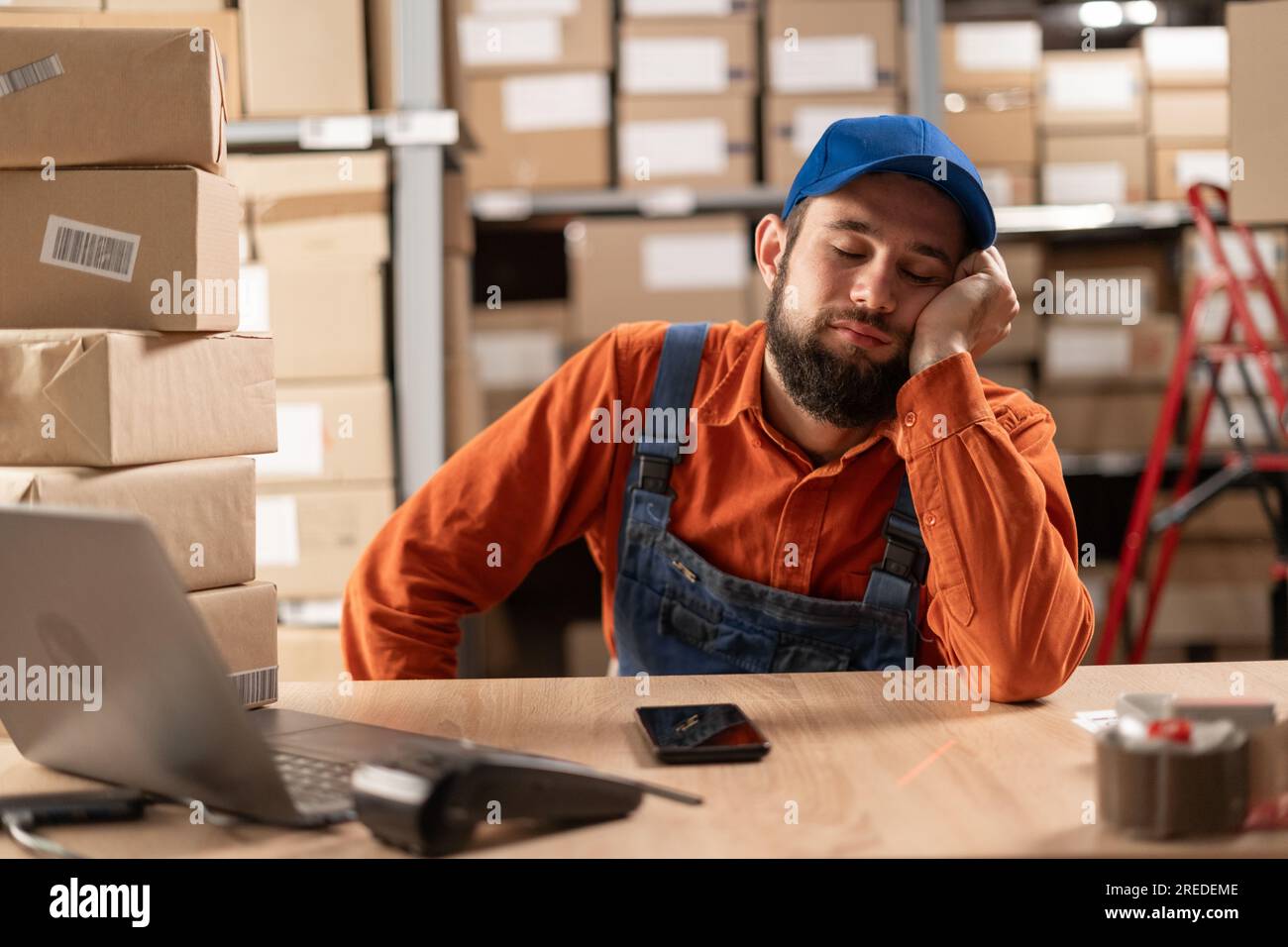 Young tired warehouse worker sleeping at workplace exhausted from ...