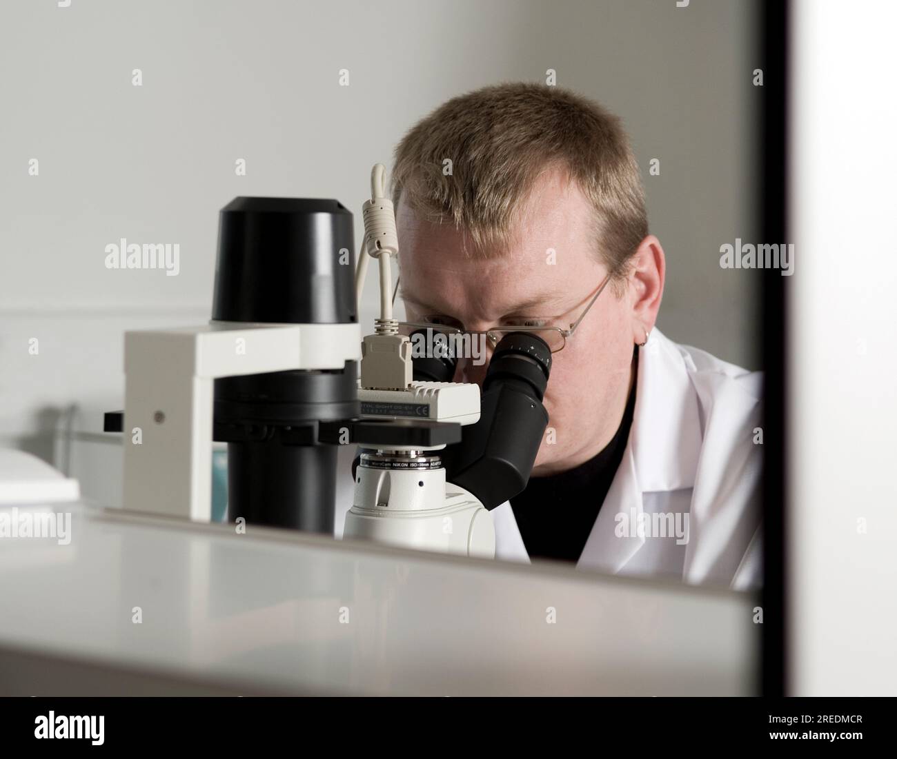 A scientist in a white lab coat looks through a microscope in a clean ...
