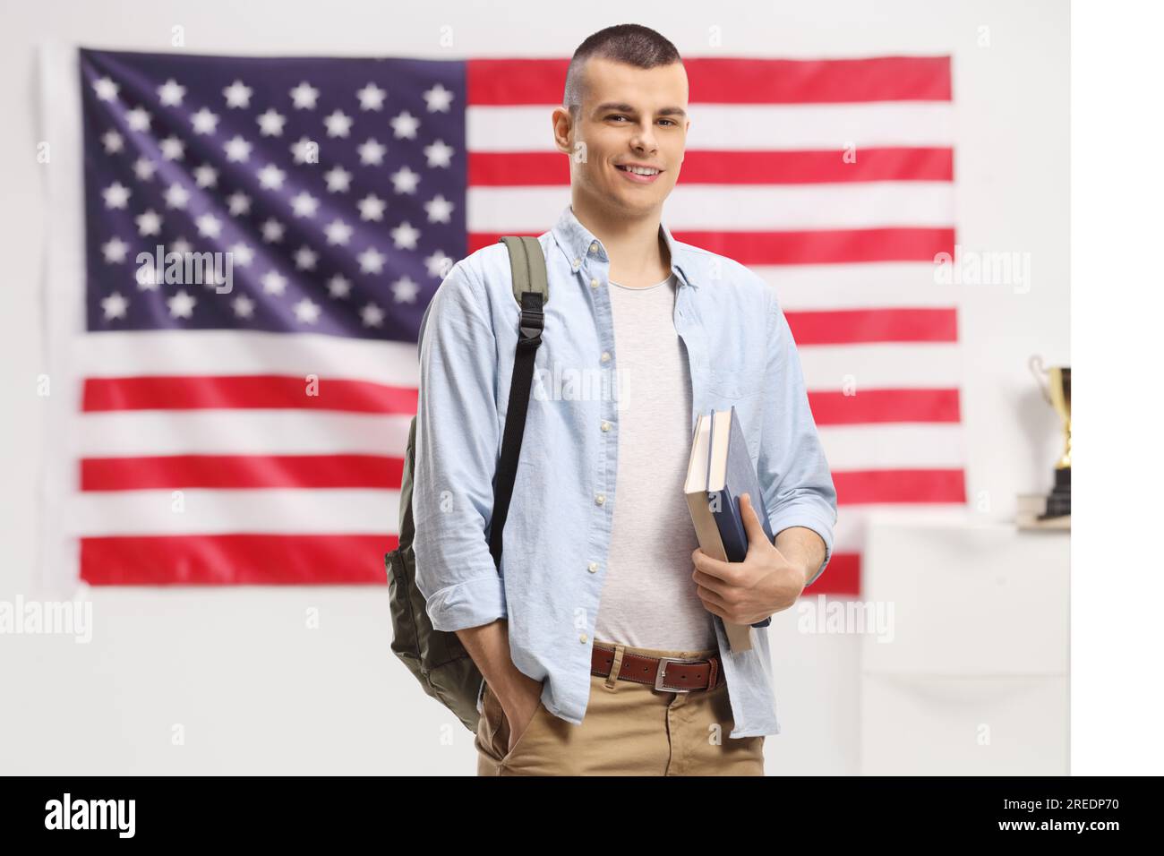 Male student with books and backpack smiling in front of a USA flag ...