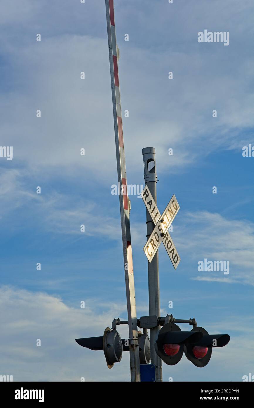 Railroad crossing gate against blue sky in low late afternoon sun. Sun ...