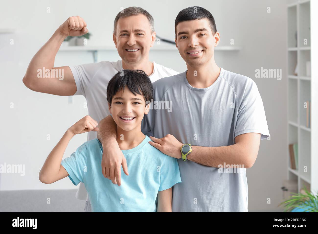 Happy young man with his little son and father showing muscles at home ...