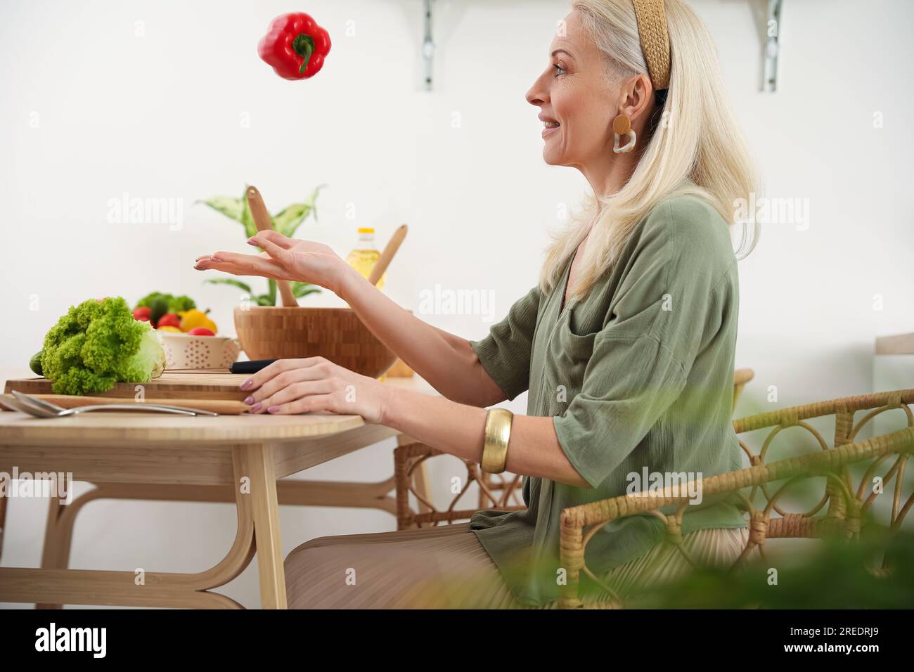 Mature woman throwing bell pepper at table in kitchen Stock Photo - Alamy