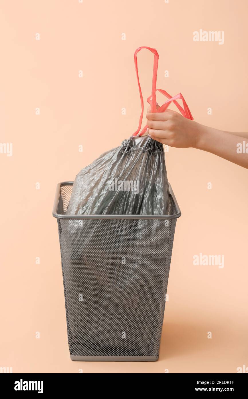 Female hands taking full garbage bag from trash bin on beige background ...