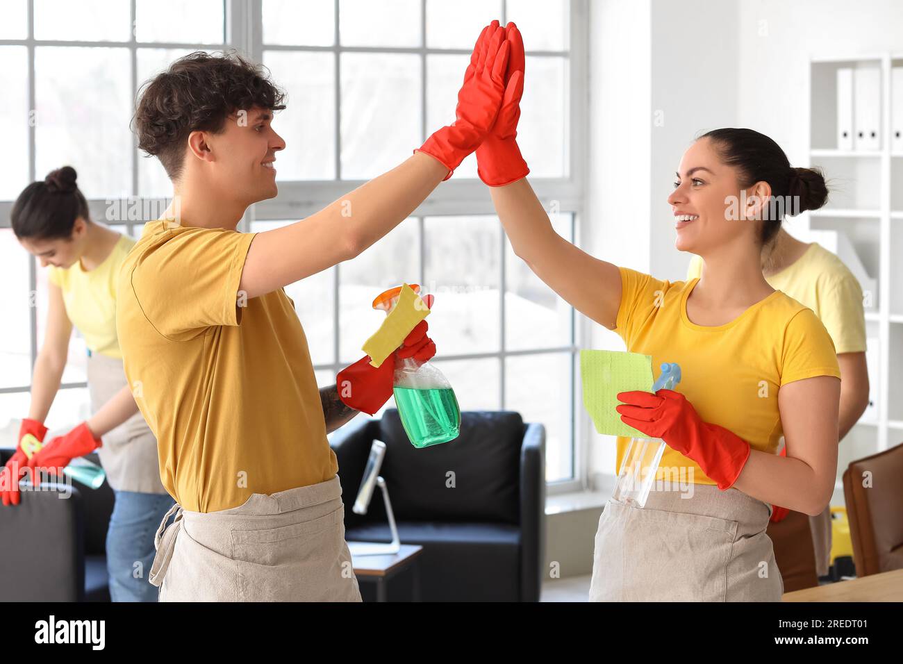 Young janitors with cleaning supplies giving each other high-five in ...