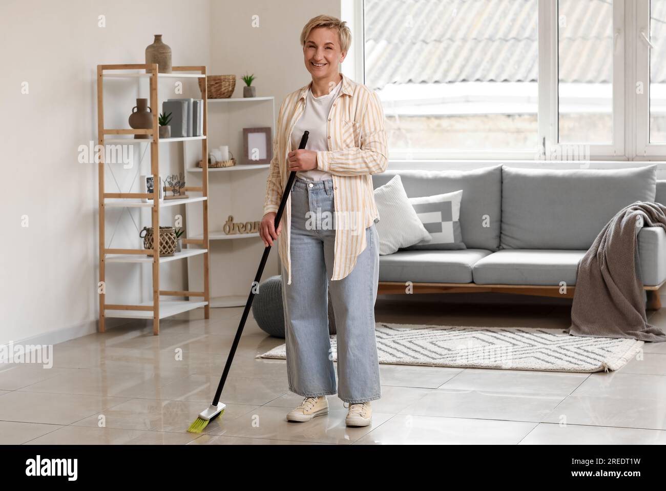 Mature woman sweeping floor in room Stock Photo - Alamy