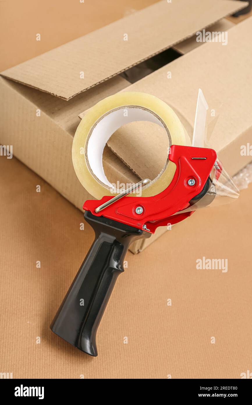 Packing tape dispenser and cardboard box on beige background Stock ...