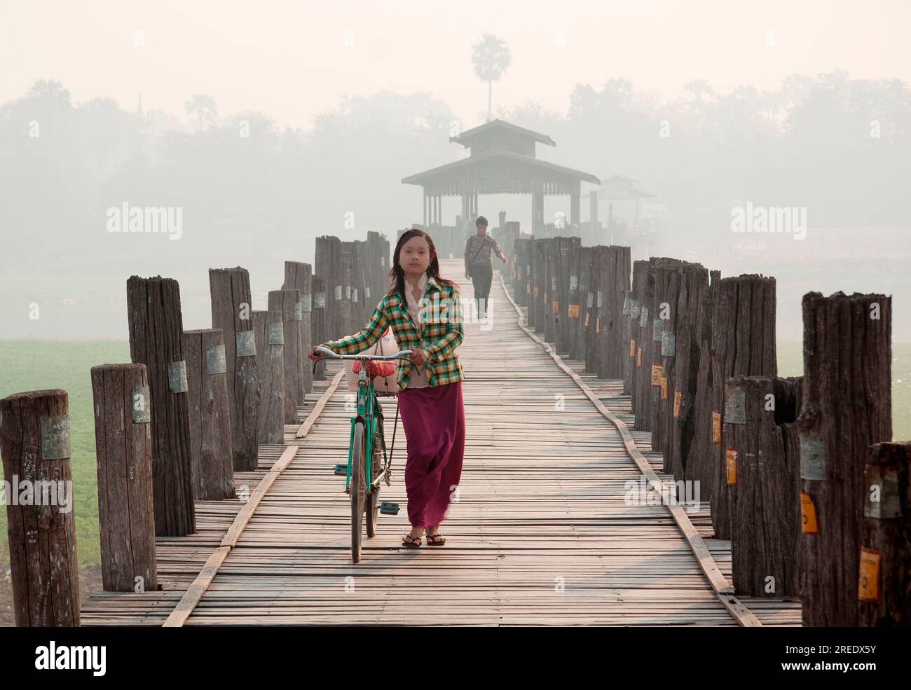 A young Burmese woman walking over the Ubein Bridge with a bicycle ...