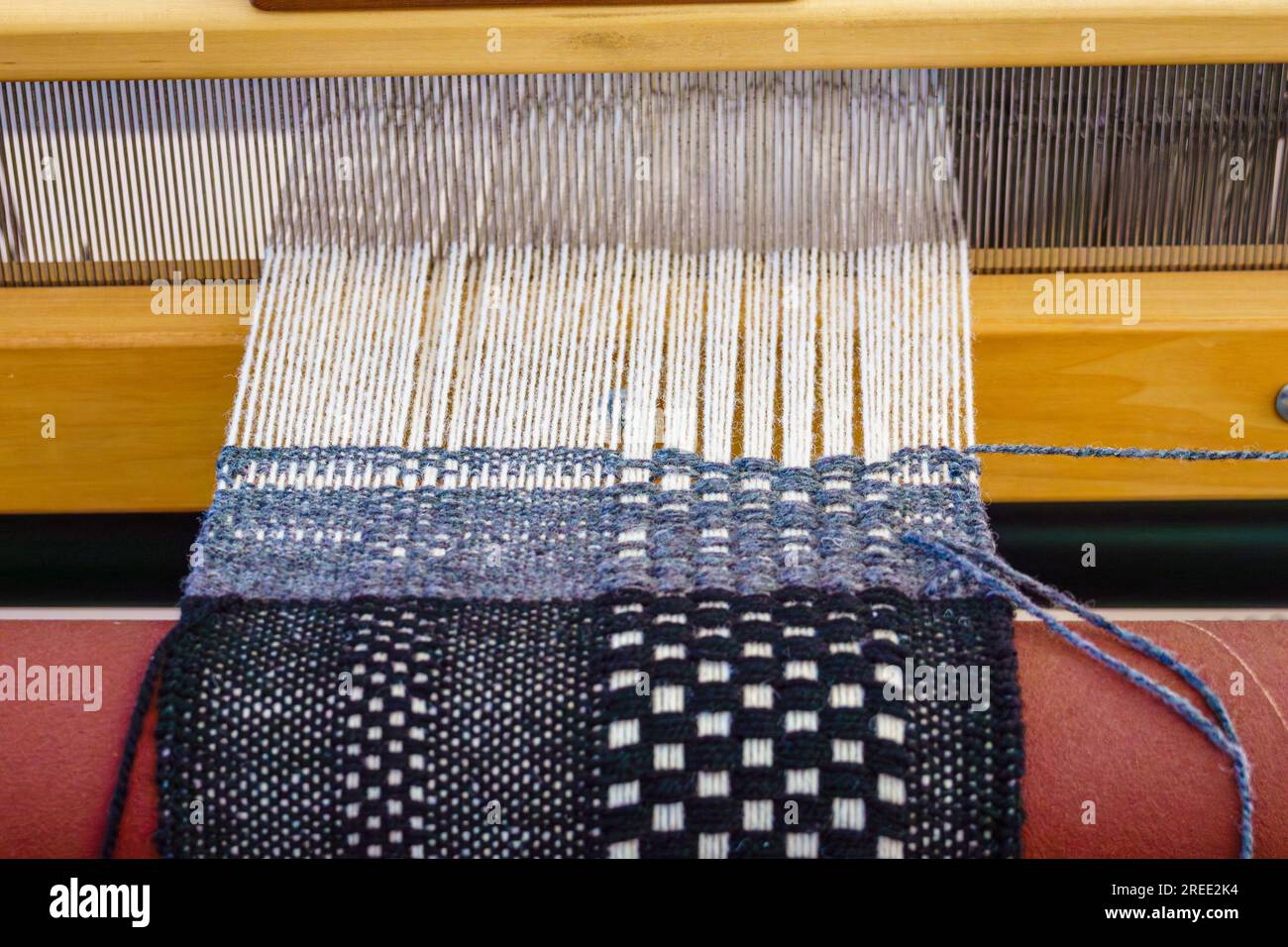 Close-up of a floor loom with black white and blue hand-woven textiles ...