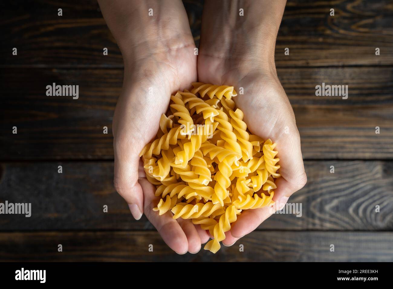 Raw uncooked Italian pasta fusilli held in two hands over a dark wooden ...
