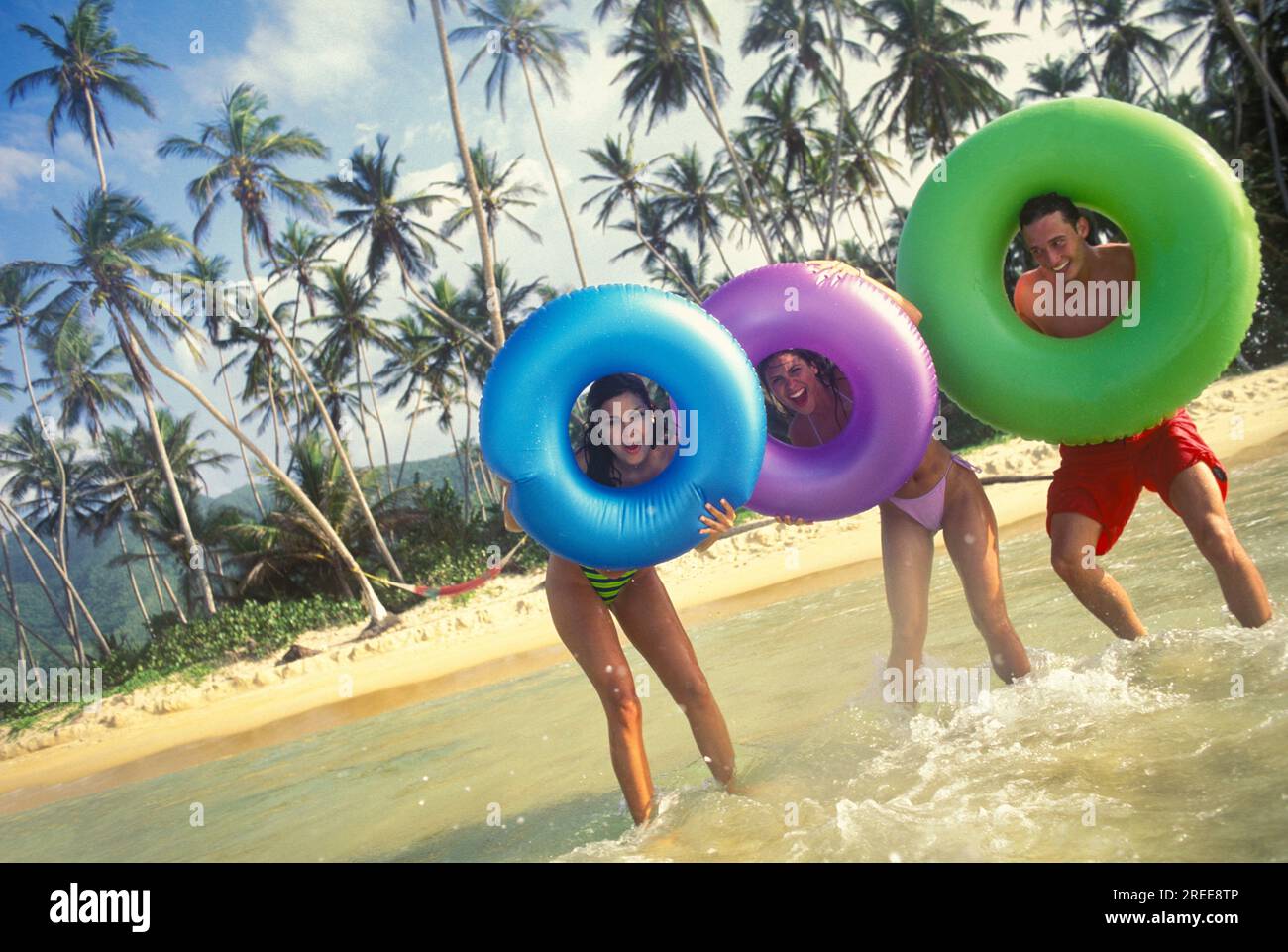 Three young adults holding inflatable rings on the beach, Choroní ...