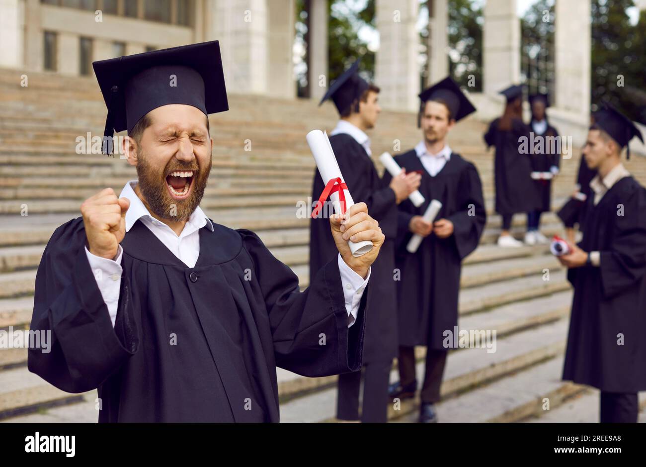 Happy joyful male university graduate in cap and gown celebrating his ...