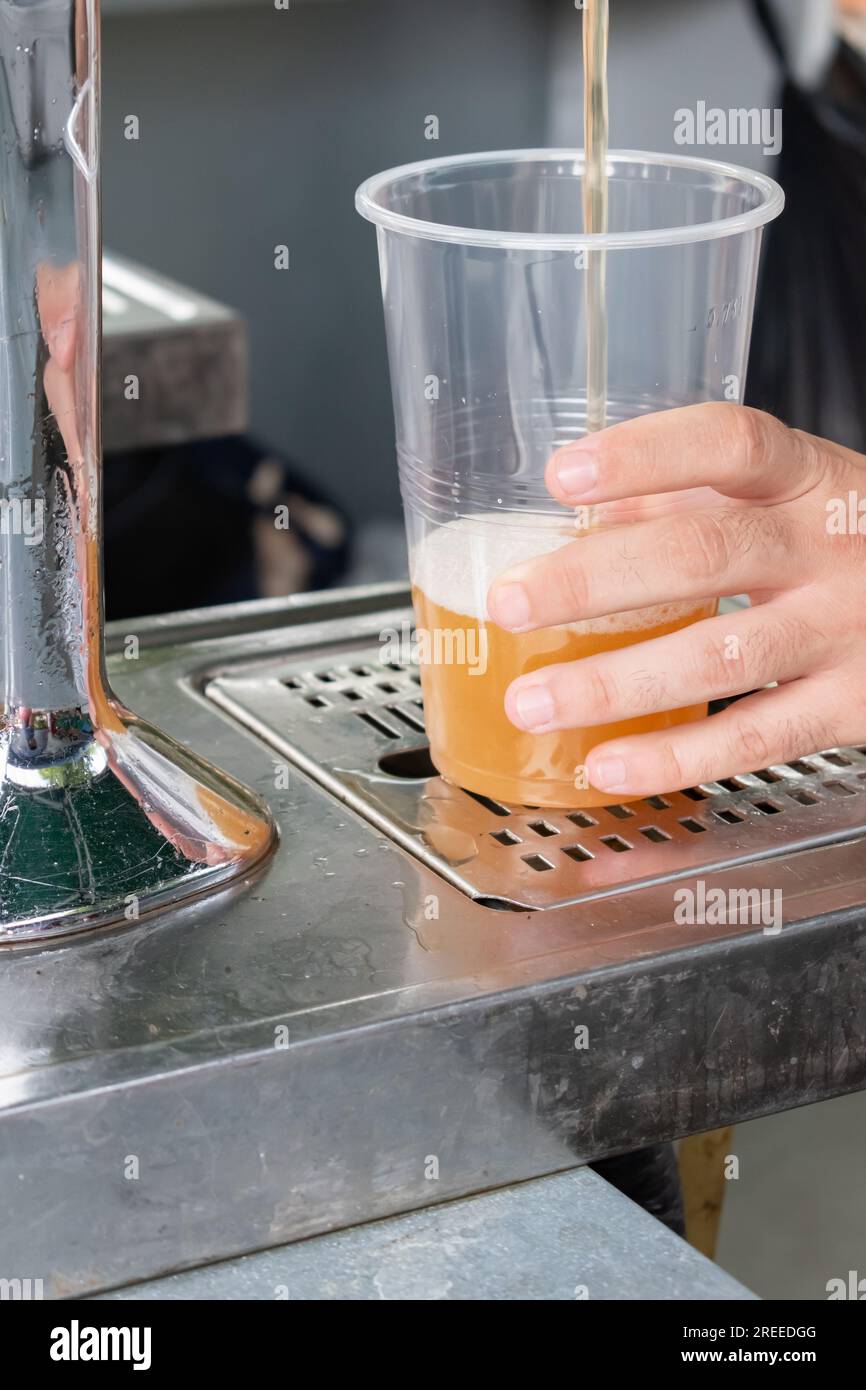 Detail of a man filling a plastic glass of beer at a street stand ...